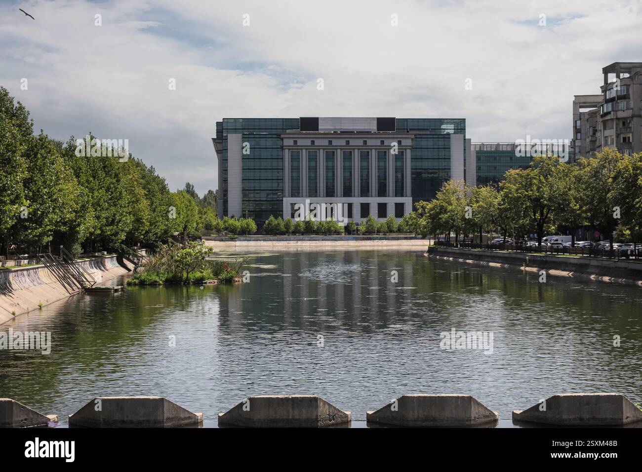 A peaceful view of a river, surrounded by trees and modern architecture ...