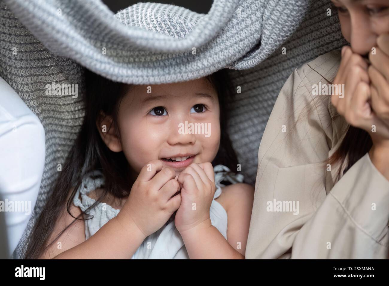 Child excitedly hiding under a blanket with family, sharing a playful ...