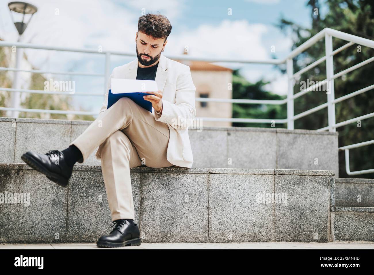 Young man reading a document while sitting on outdoor steps Stock Photo ...