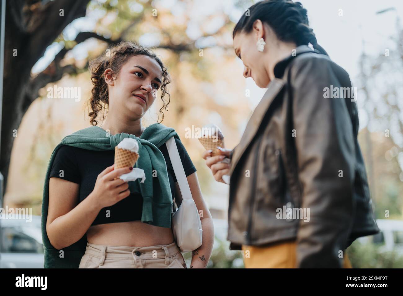 Two women enjoying ice cream with joyful facial expressions outdoors ...