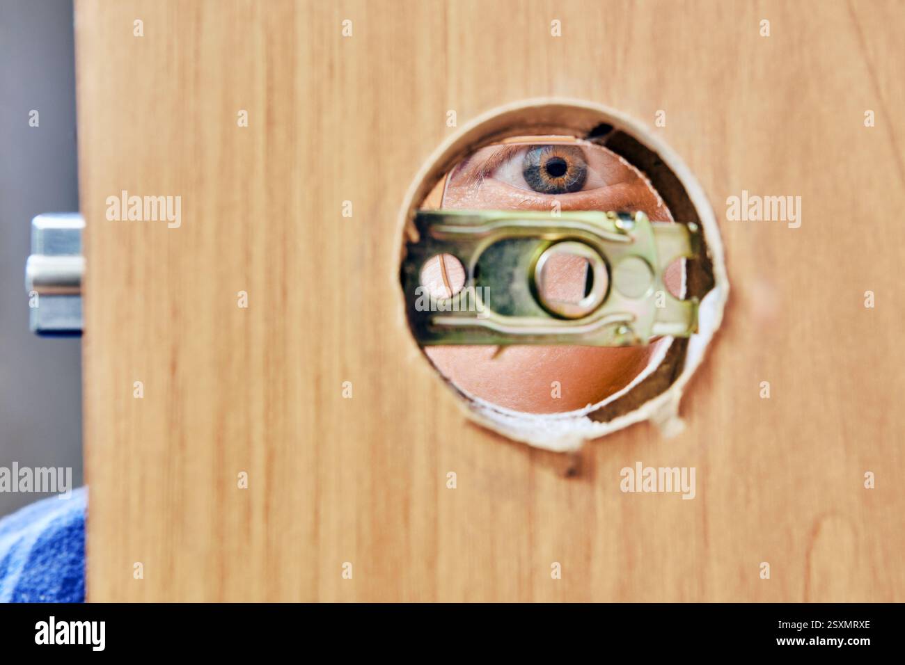 Door bore reveals human eye looking through rough cut opening with ...