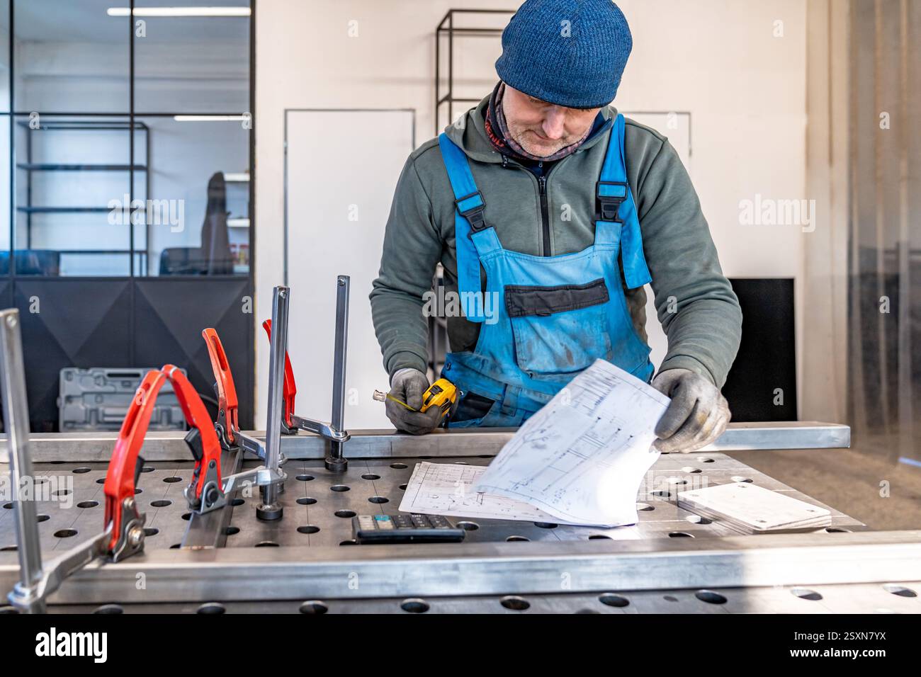 Metalworker reading technical drawings and using measuring instruments ...