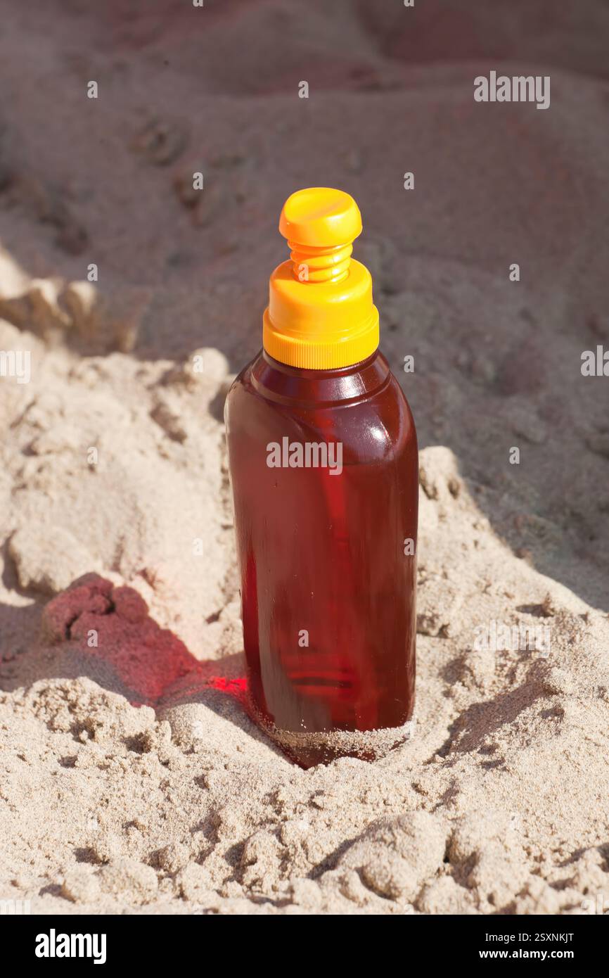 Bottle of suntan lotion resting in the warm sand at the beach, soaking ...