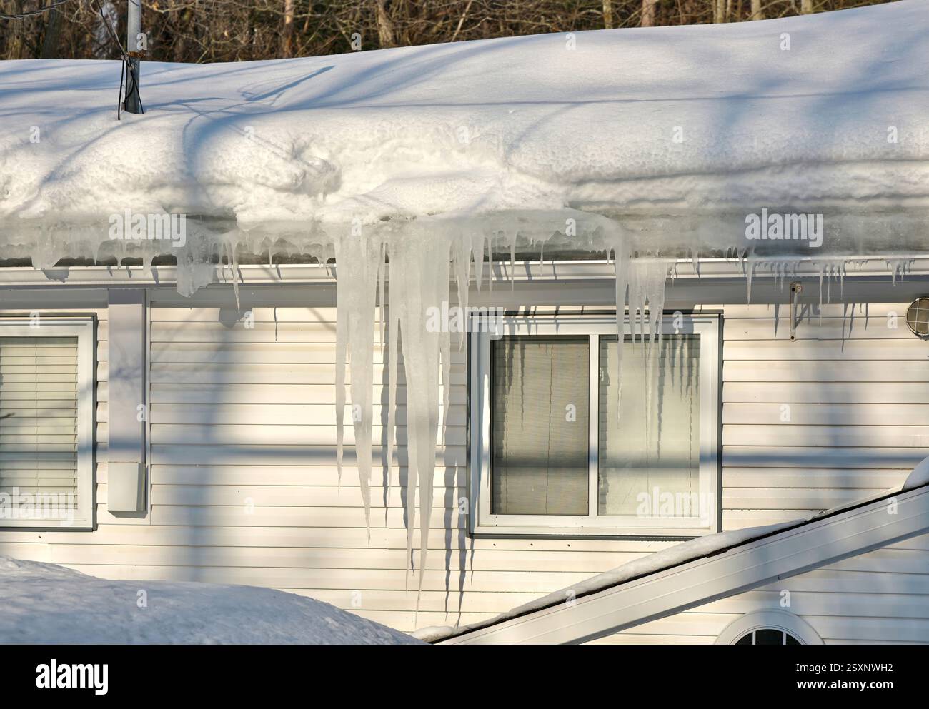 Large icicles and ice dams form at the edge of the snow-covered roof ...