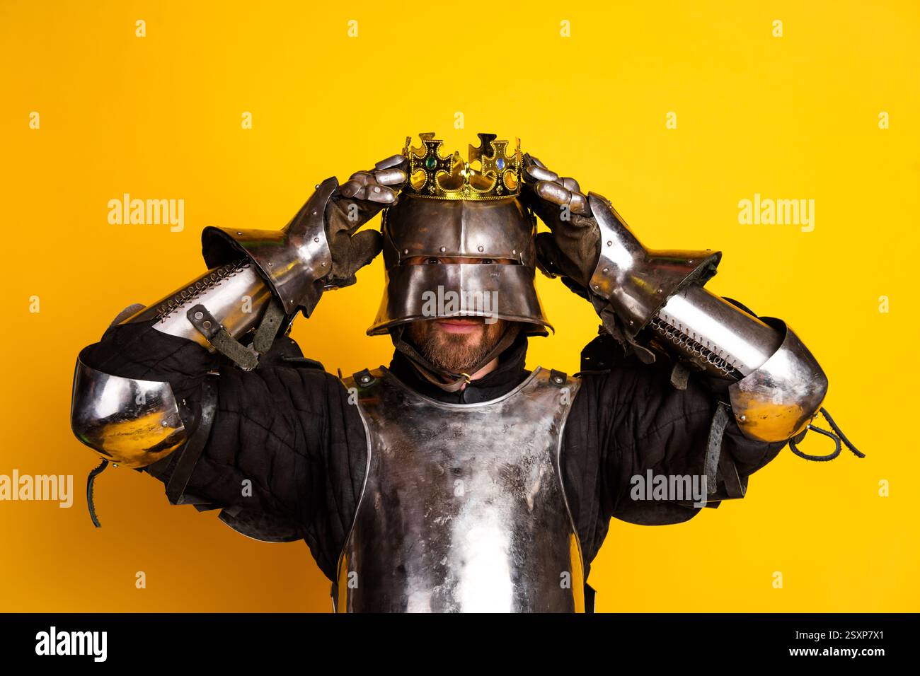 A young man in medieval armor poses with a crown against a vivid yellow ...