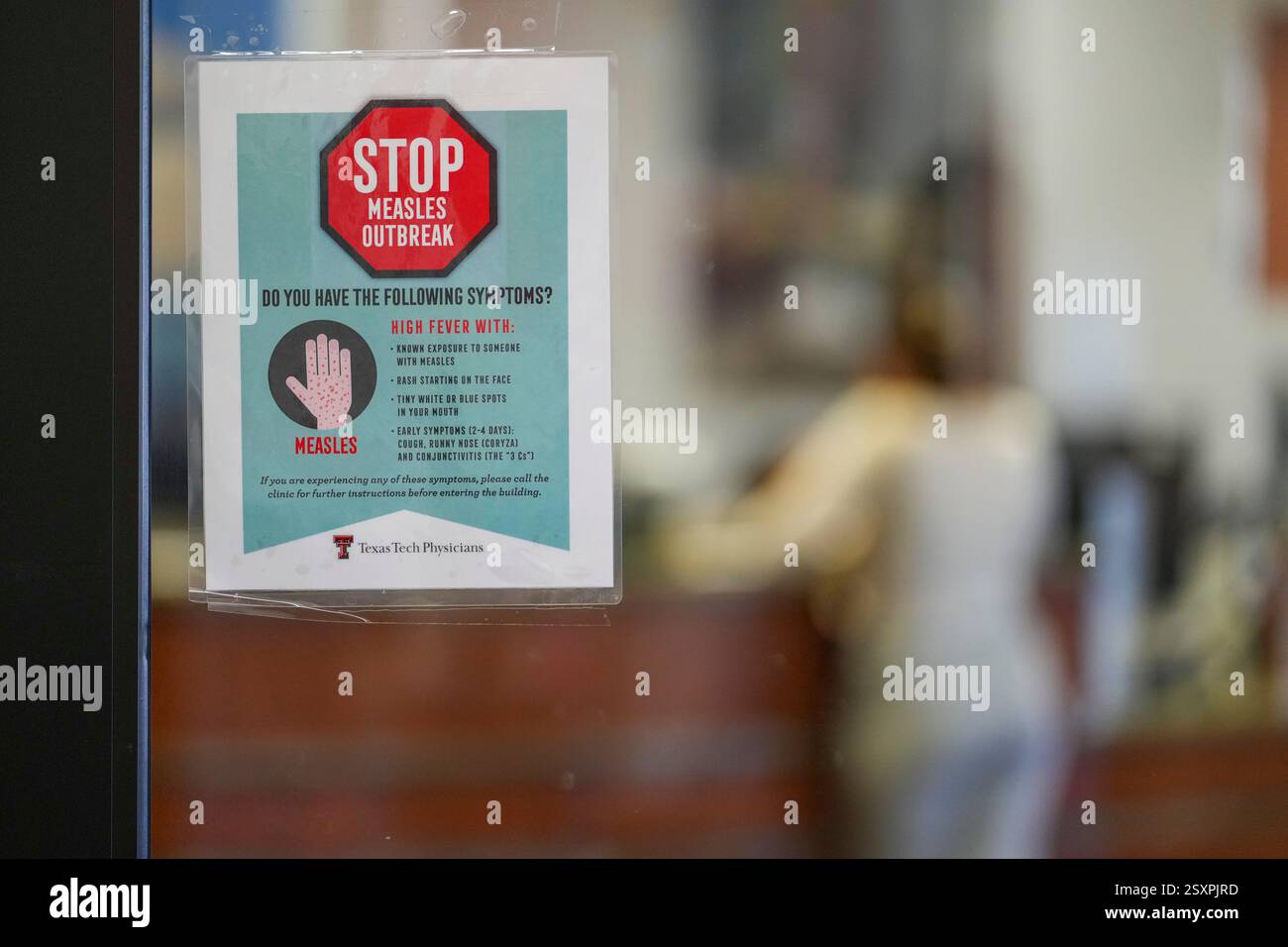 A sign warning of measles is posted on a glass door as a patient checks ...