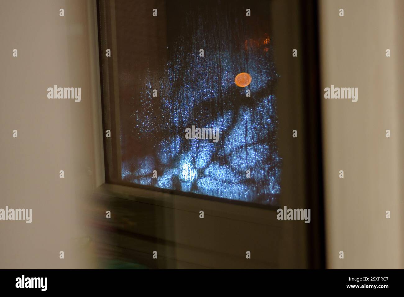 Softly illuminated colors bleed through a rain-streaked window ...