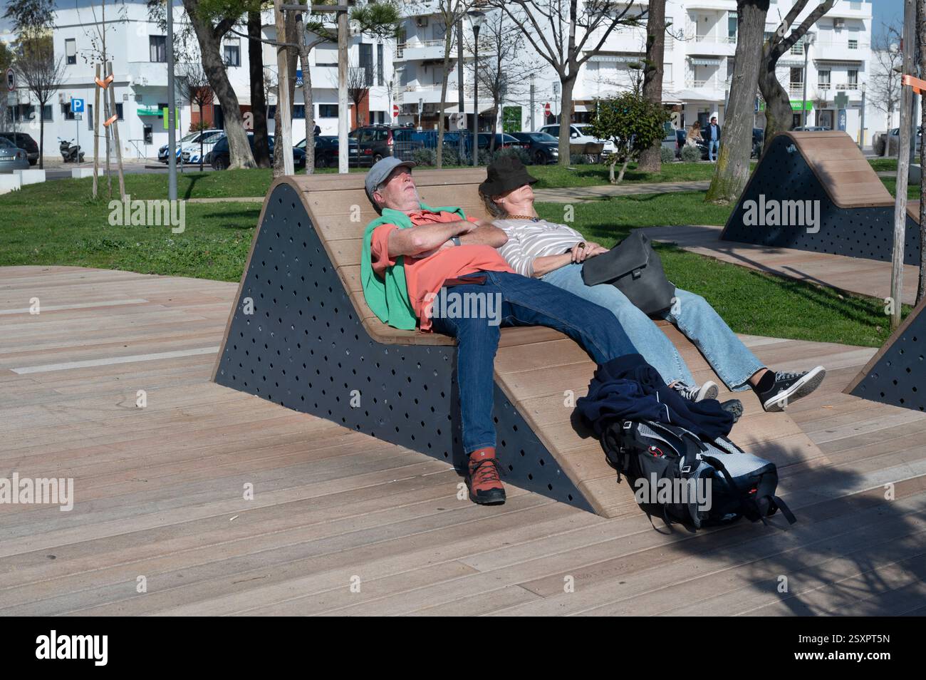 Portugal, Olhão, Algarve. Two travellers sunbathe on public seats in ...