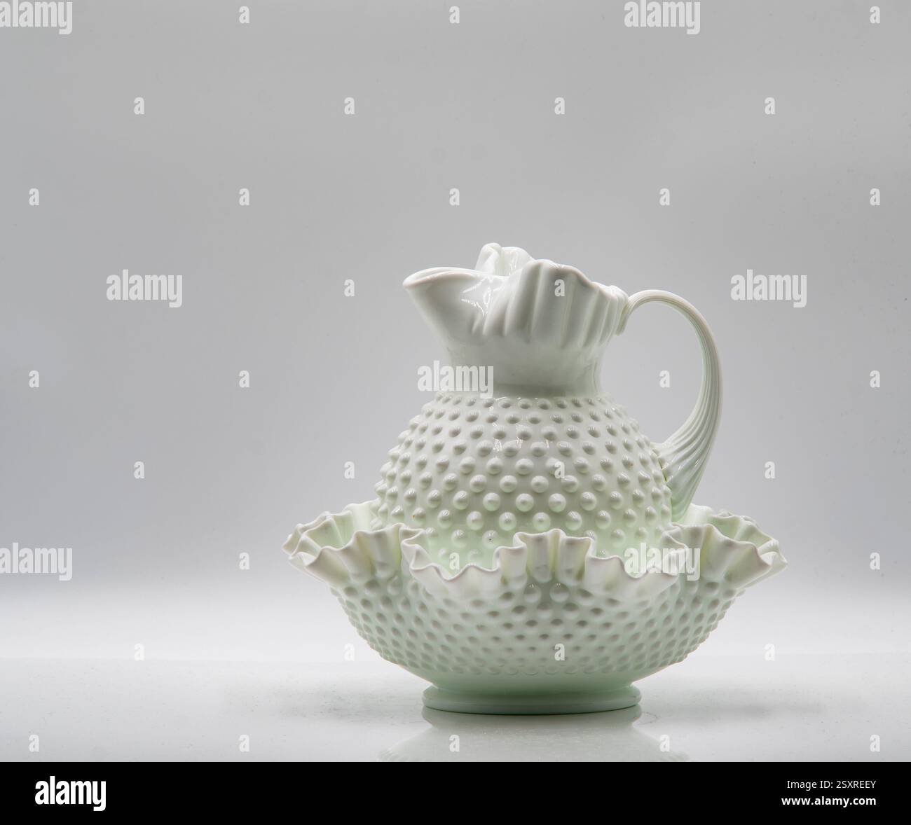 A white ceramic pitcher with a textured surface and ruffled base is ...