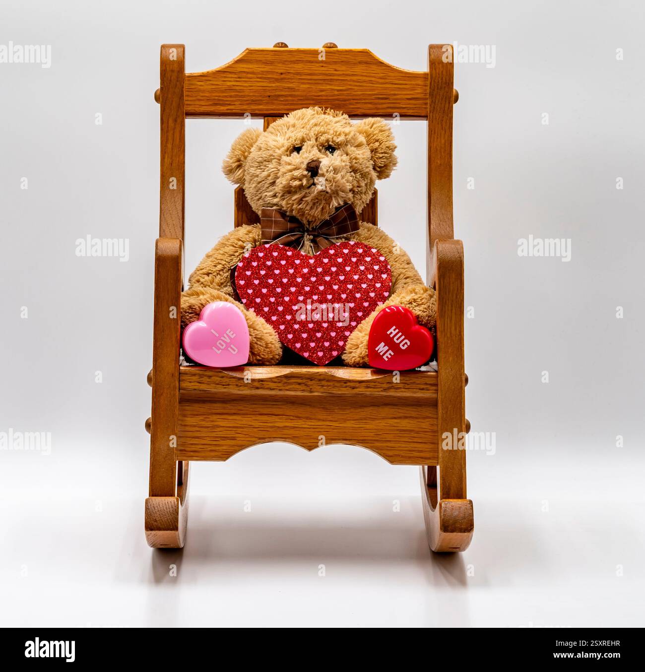 A soft teddy bear sits in a small wooden rocking chair, holding heart ...