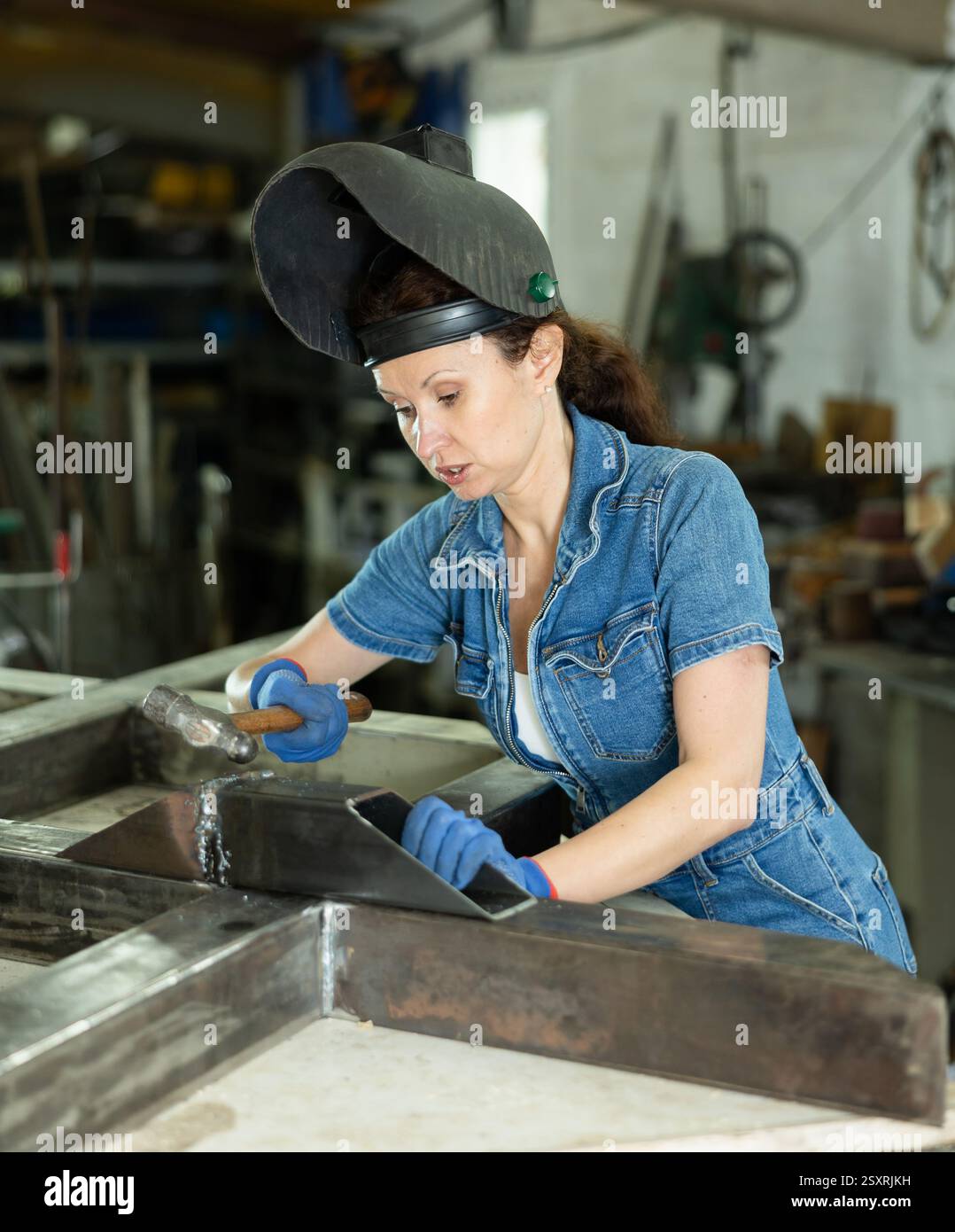 Portrait of a female welder standing with a welding semi-automatic machine and a safety helmet ...