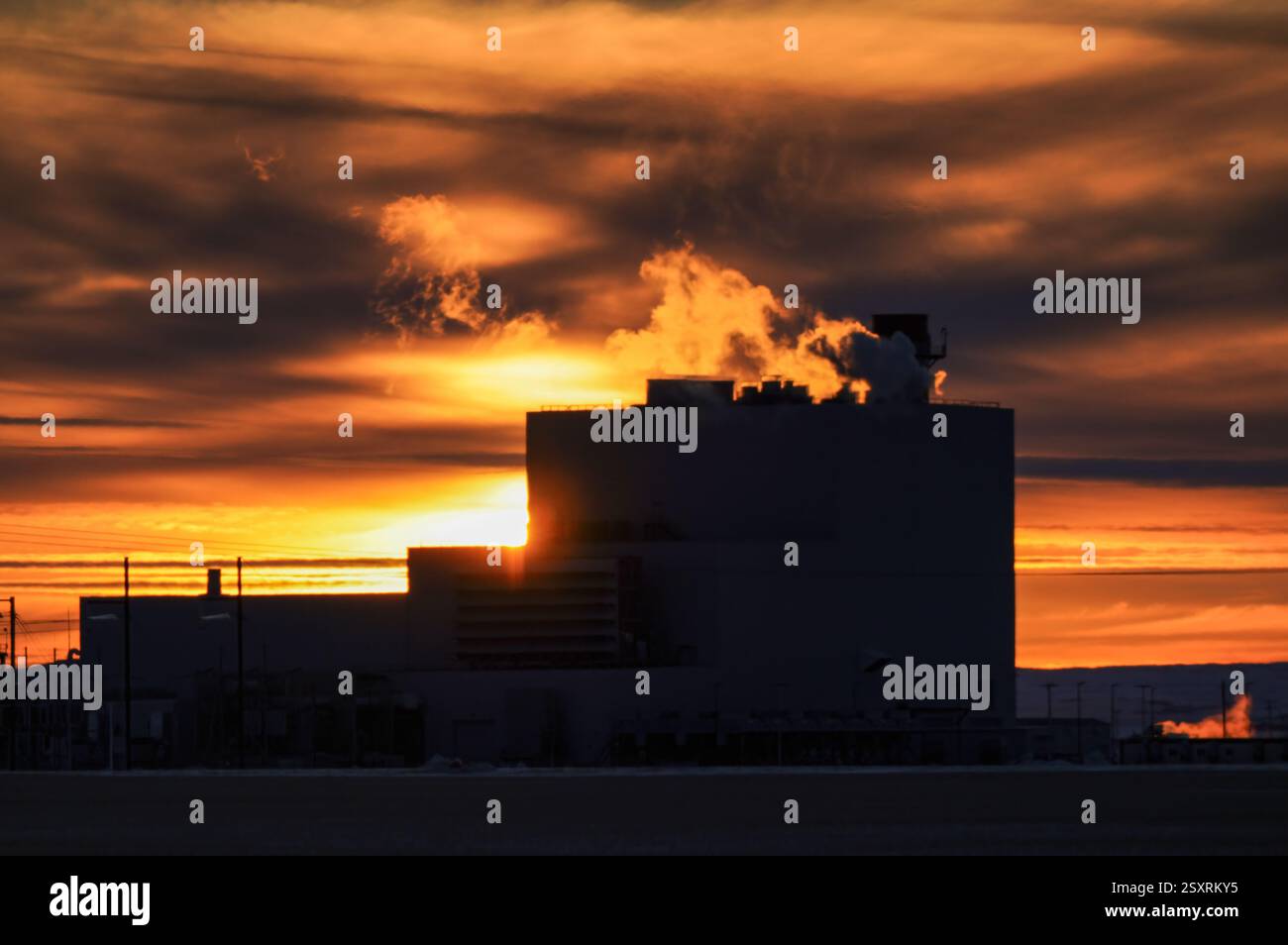 Smoke billowing from an industrial building at sunrise creates a ...