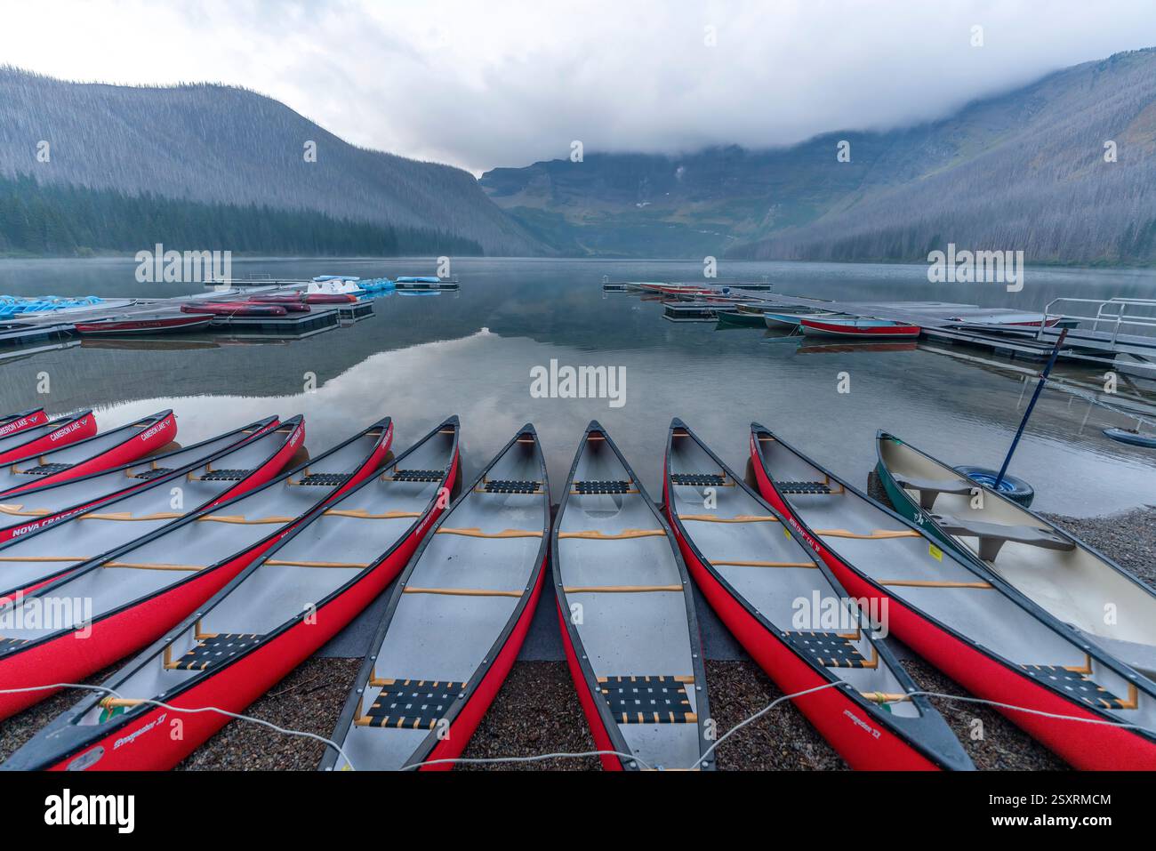 Red canoes are lined up on the shore of lake josephine in glacier national park, montana, ready ...