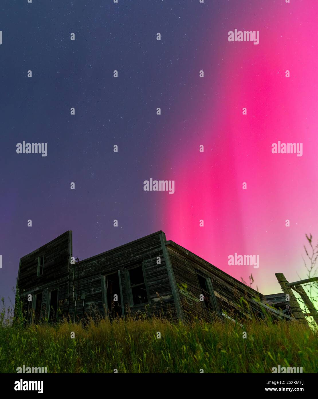 Vibrant pink aurora borealis lights up the night sky over an old ...