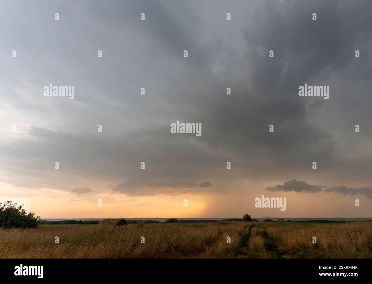 Dark storm clouds gathering over a peaceful field at sunset, creating a ...