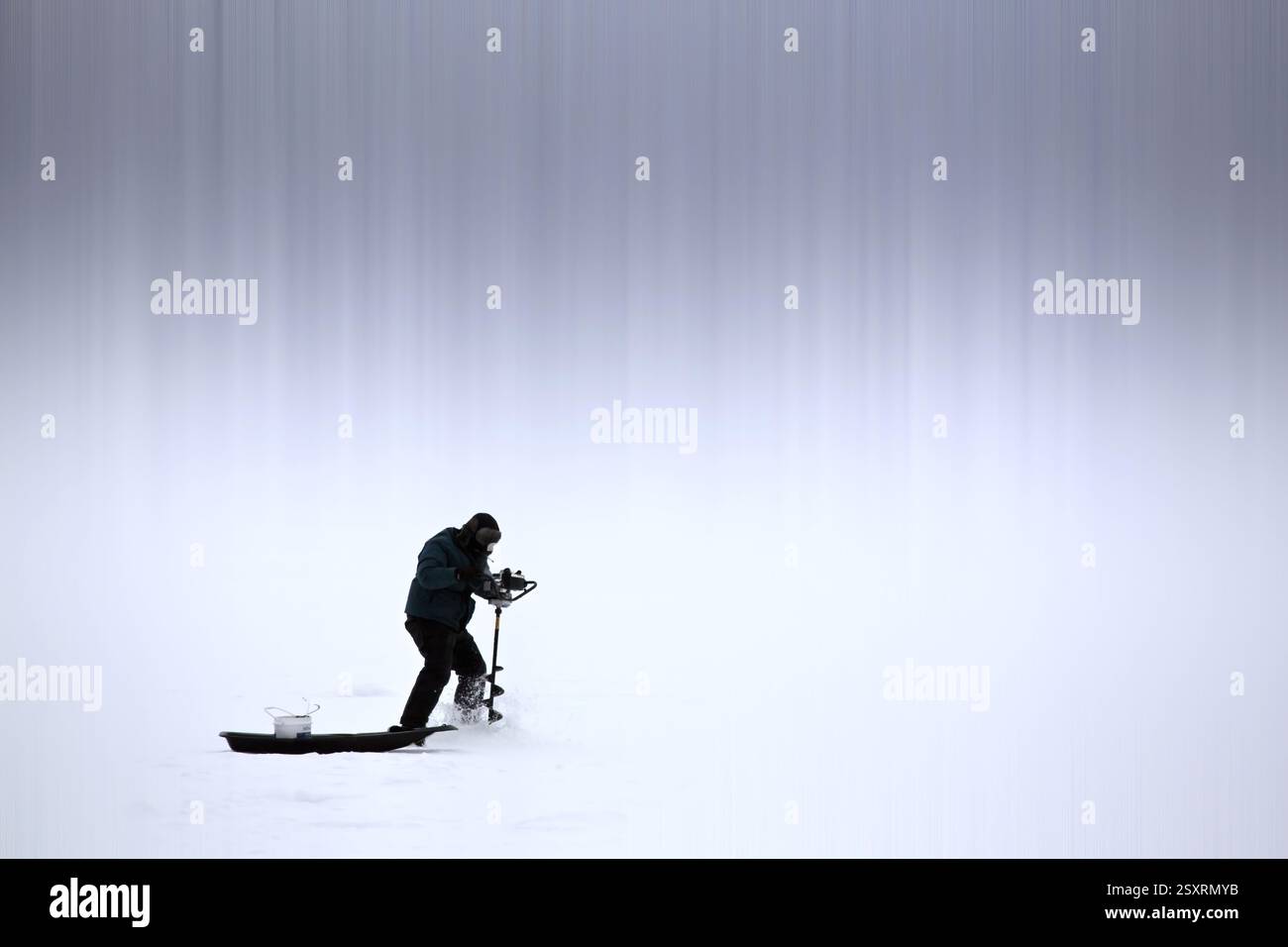 Ice fisherman drills a hole in the frozen lake surface using a hand ice ...