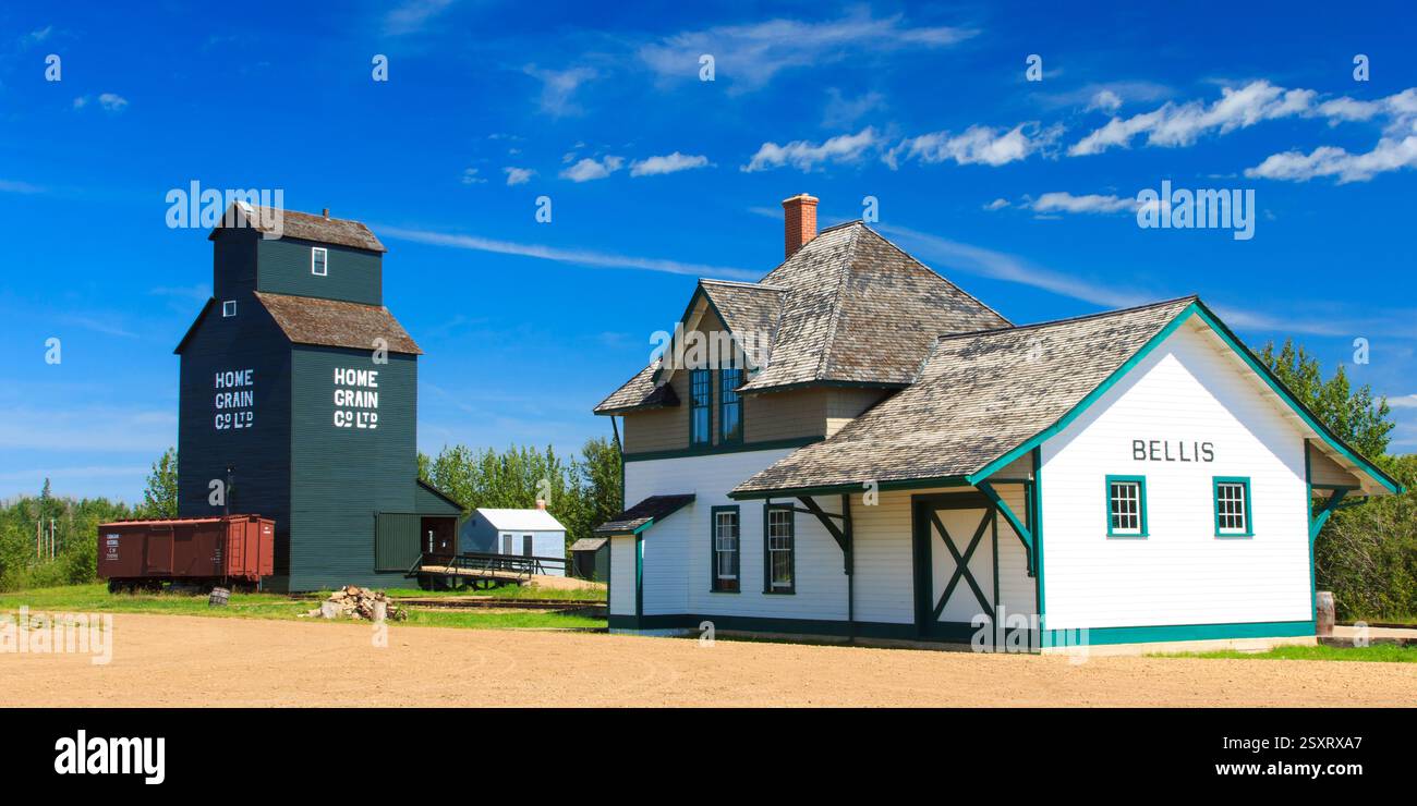 Large grain silo is next to a small house. The house is white and has a ...
