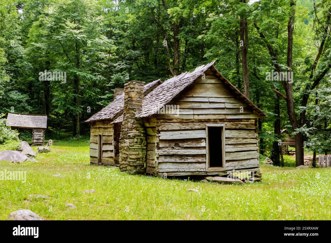 Small log cabin is in a grassy field. The cabin is old and has a stone ...