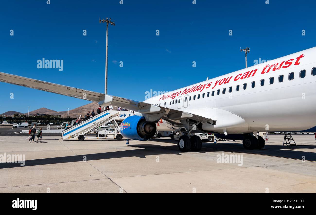 Airplane parked on airport tarmac with boarding stairs and passengers ...
