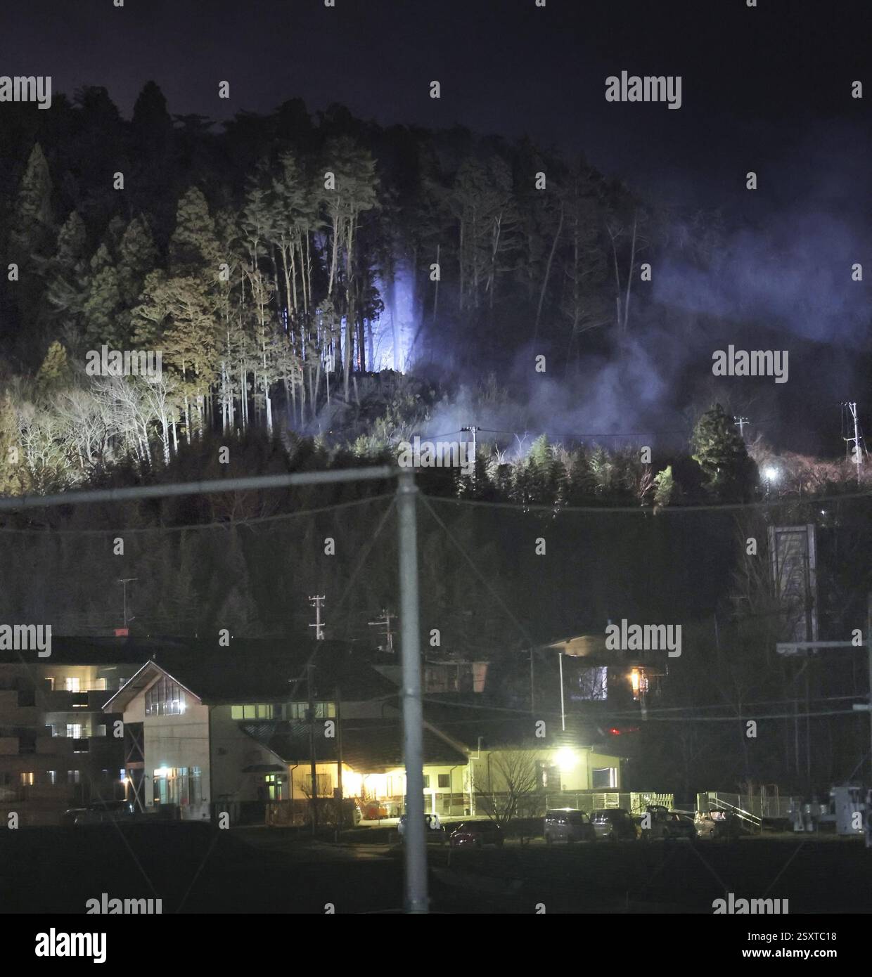 Smoke rises from a forest fire on a mountain near houses in ...