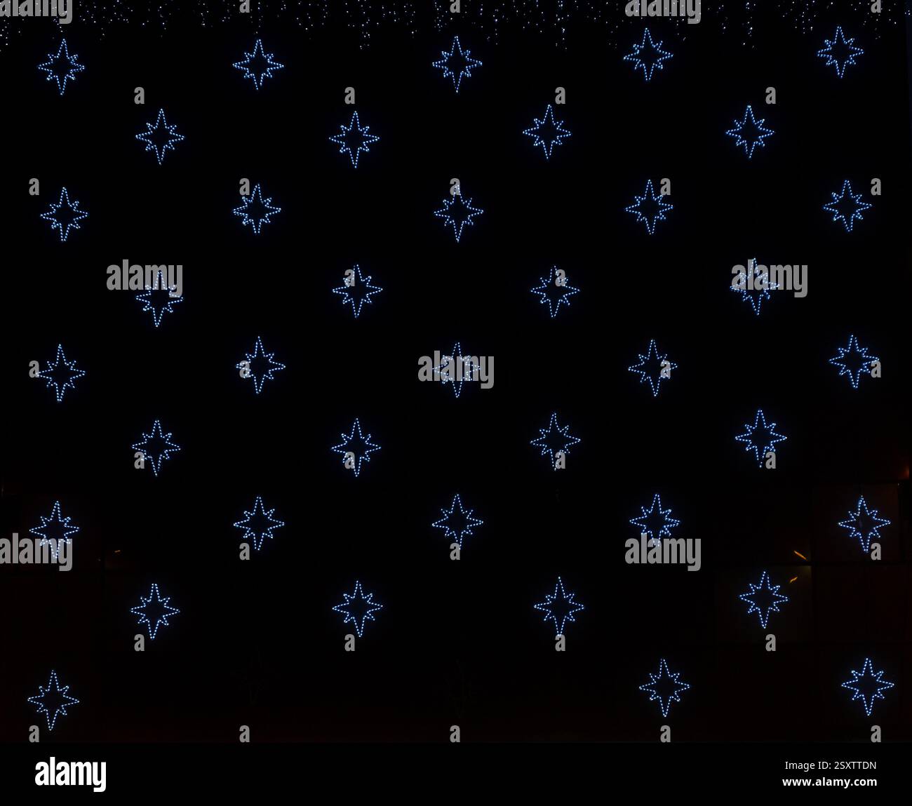 A dazzling display of blue star-shaped lights adorns a dark background ...