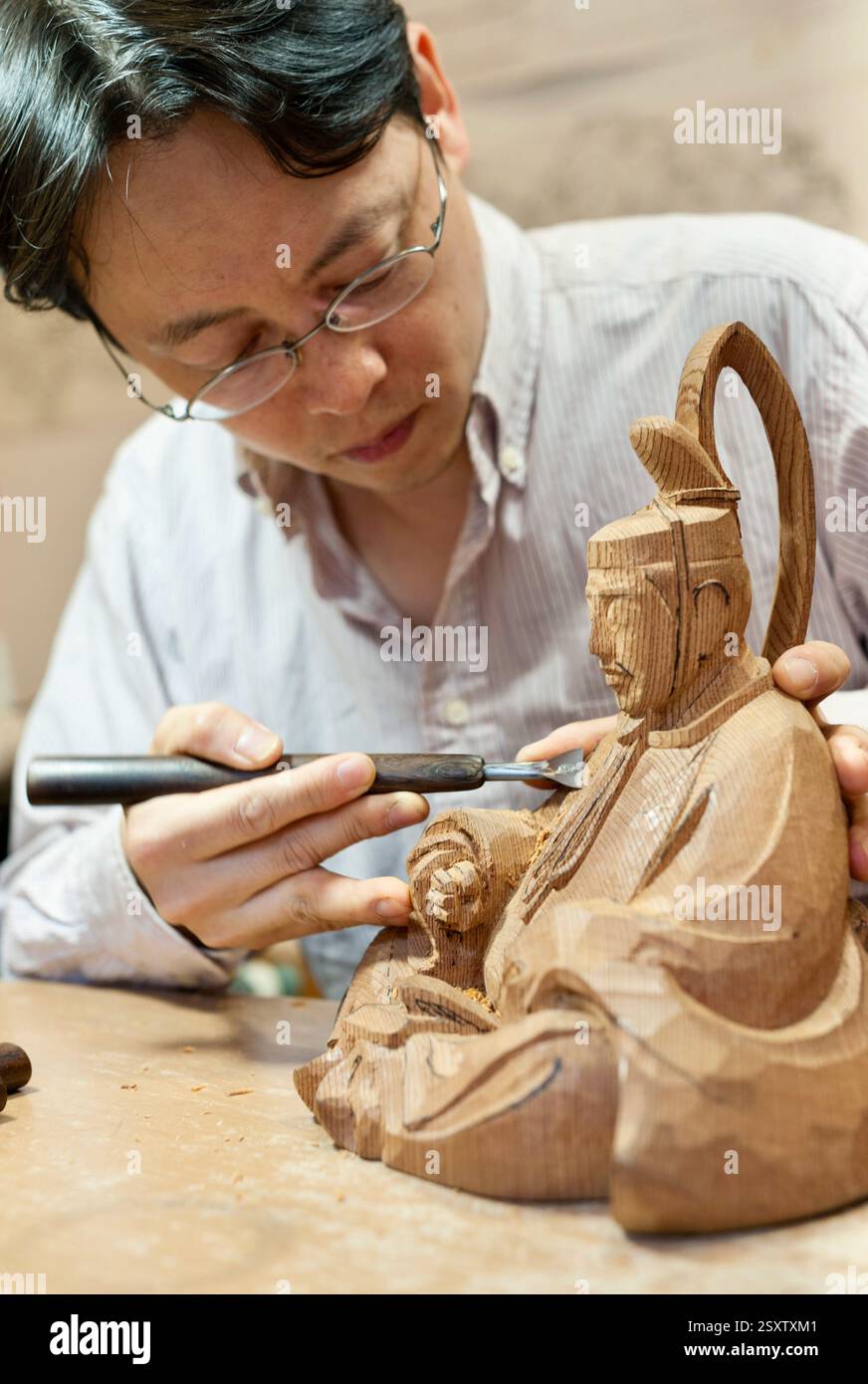 Wood sculptor Tsutomu Iwasaki carves a figurine of Tenjin-sama, a ...