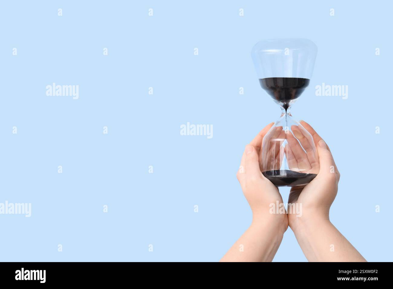 Female hands holding hourglass on blue background Stock Photo - Alamy