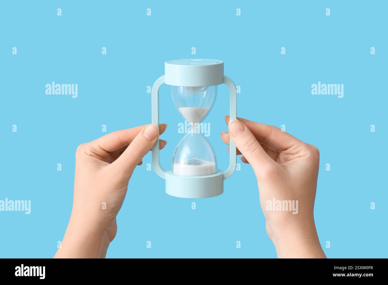 Female hands holding hourglass on blue background Stock Photo - Alamy