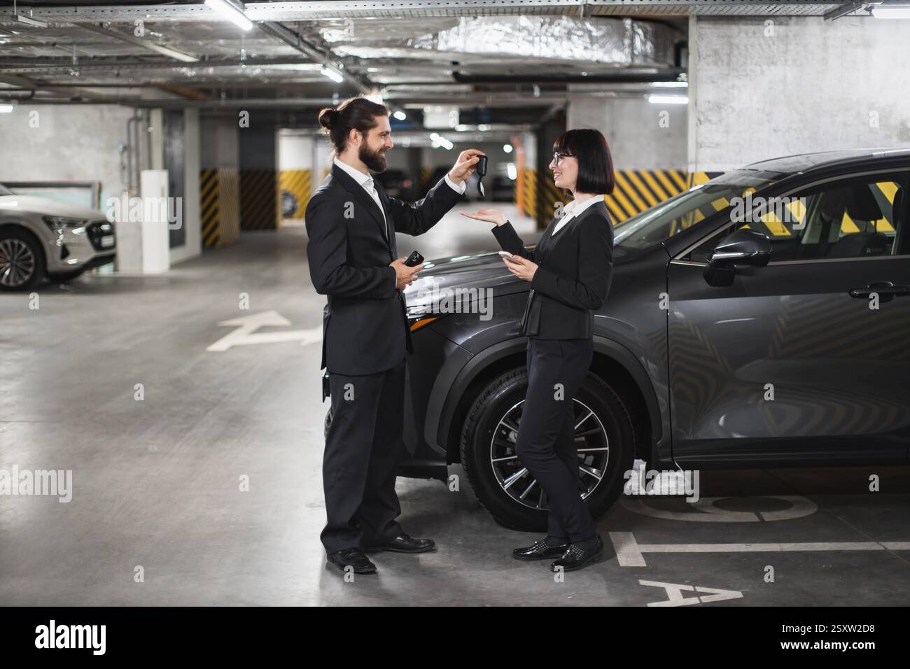 Caucasian businessman selling car to Caucasian woman in underground parking lot. Man and woman ...