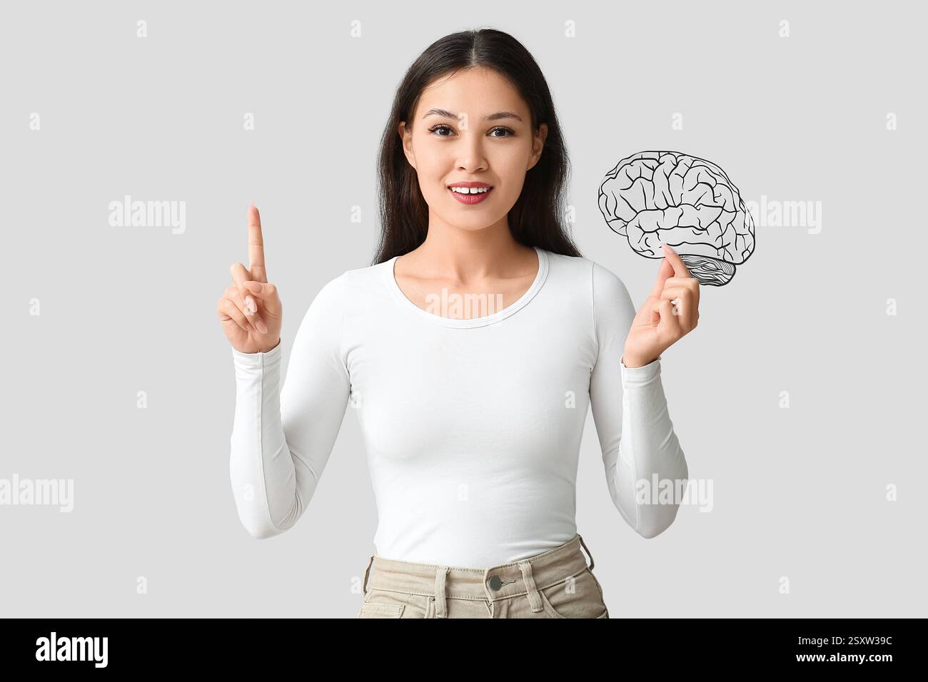 Young Asian woman with paper brain pointing up on grey background ...
