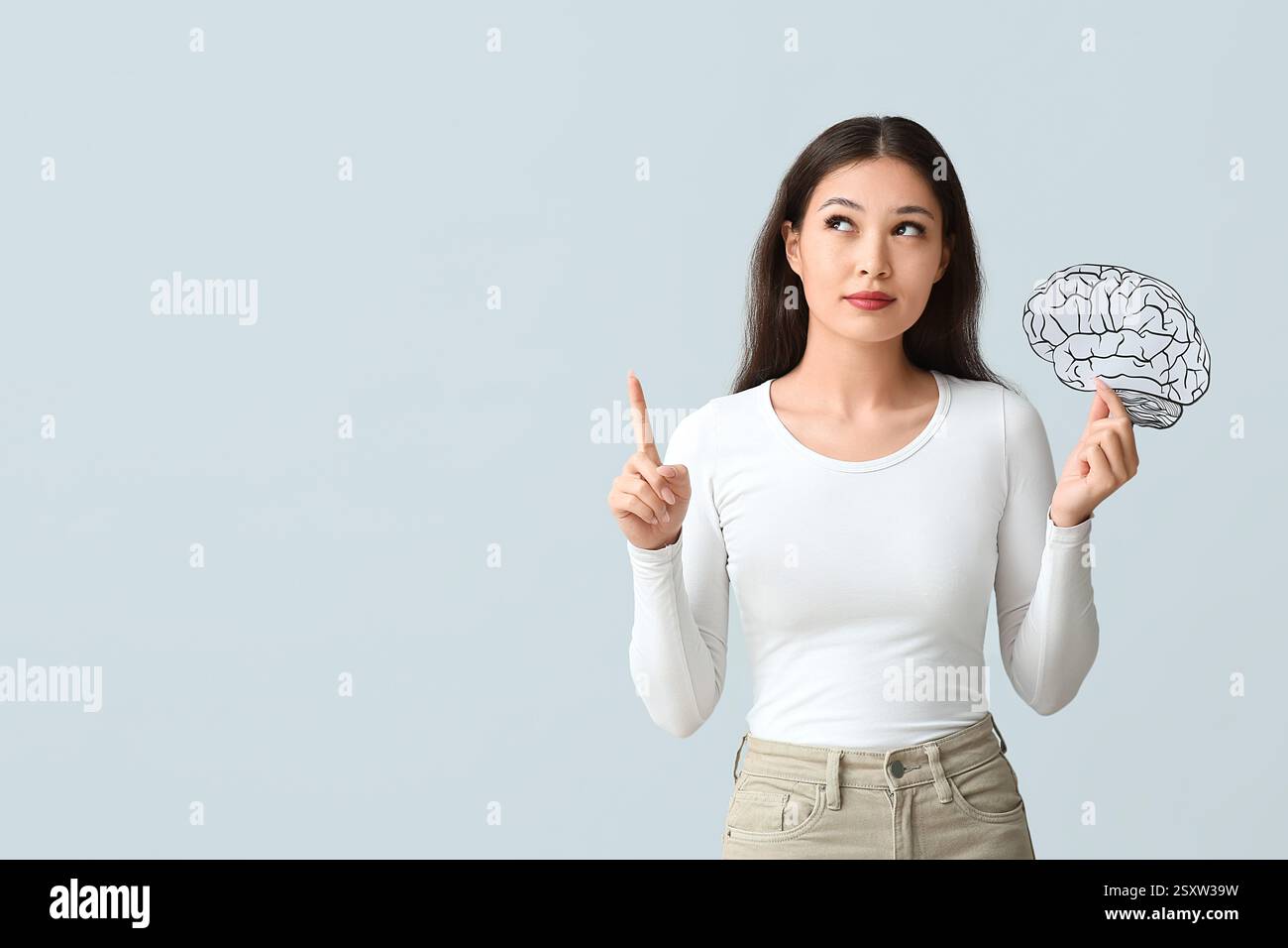 Young Asian woman with paper brain pointing up on grey background. Brain Injury Awareness Month ...