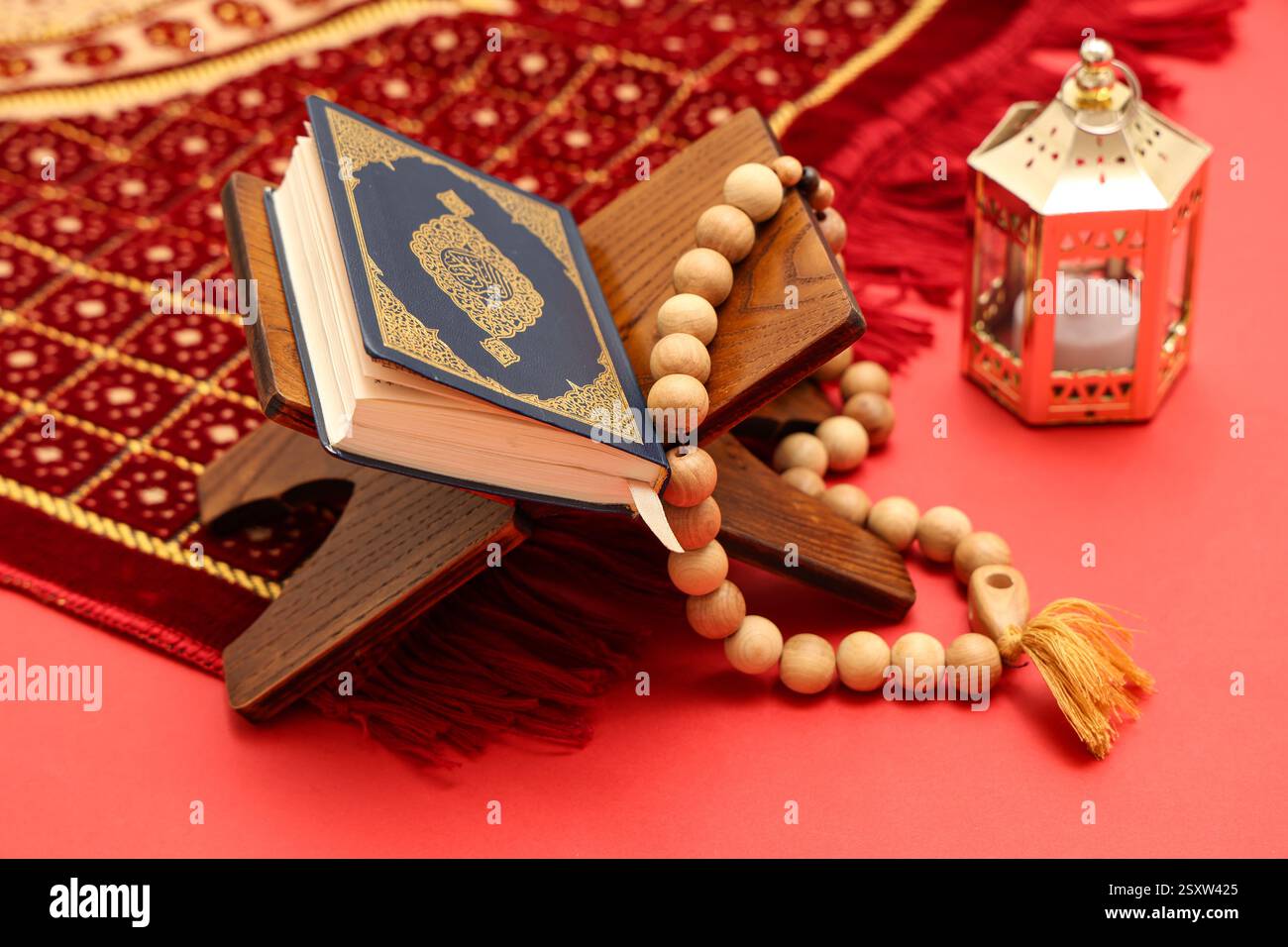 Rehal with Koran, prayer beads, rug and fanoos on red background ...