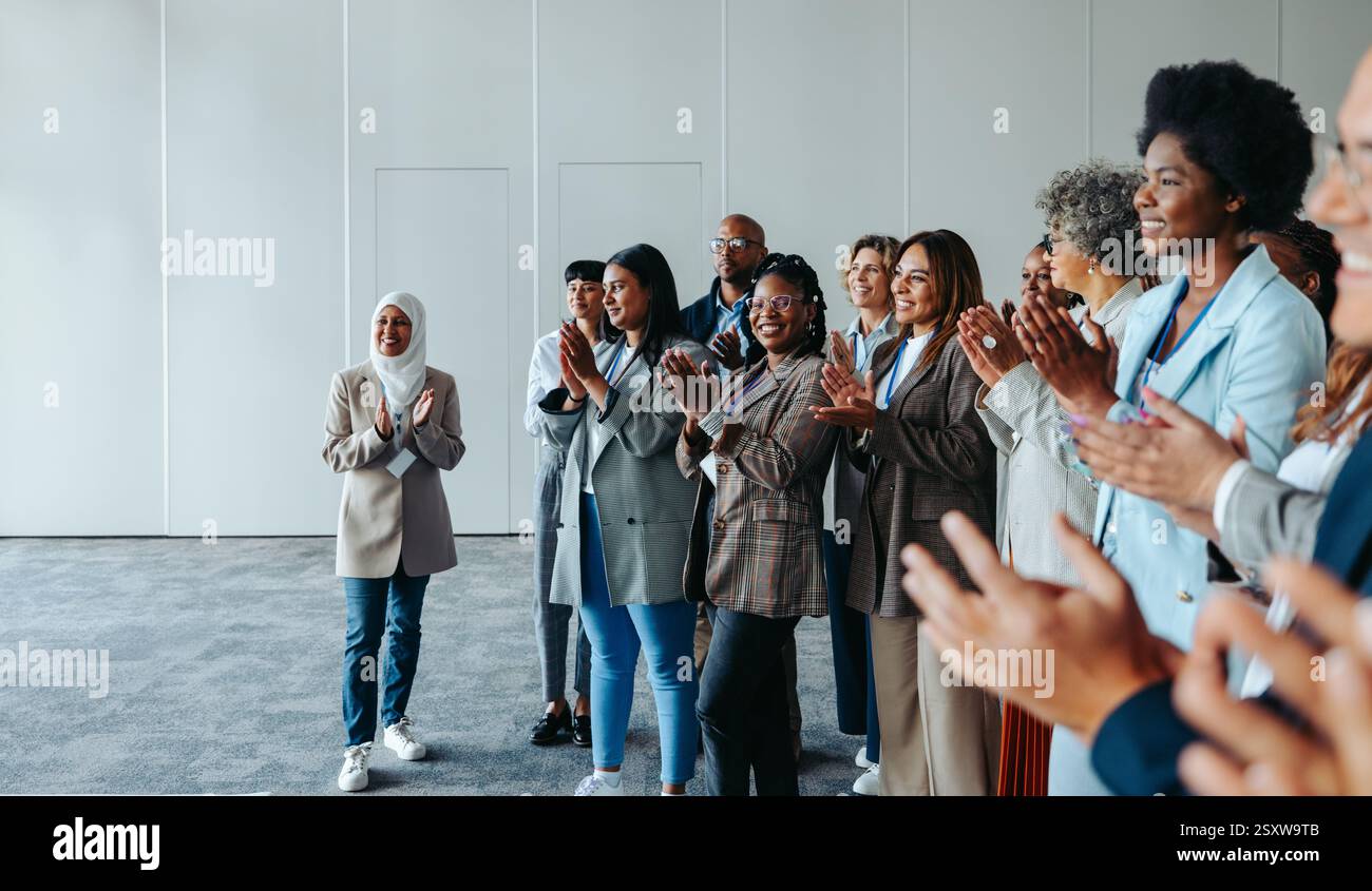 A diverse group of people at a conference clapping and smiling while ...