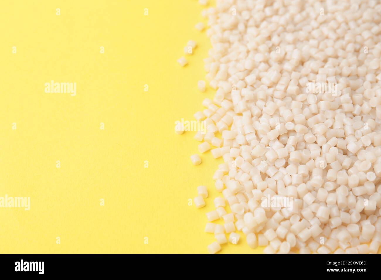Pile of plastic granules on yellow background, closeup. Space for text ...