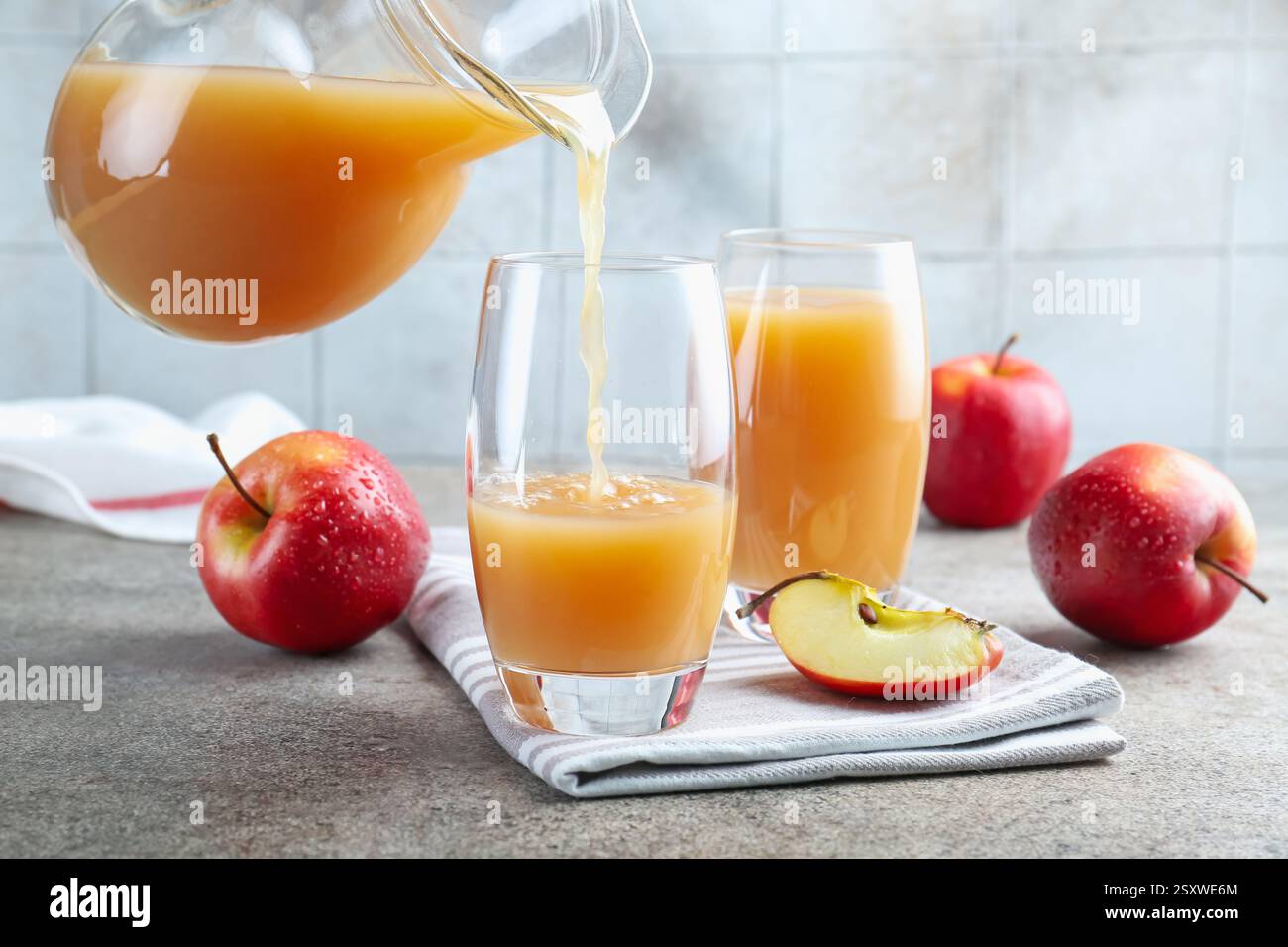 Pouring refreshing apple juice from jug into glass at grey textured ...
