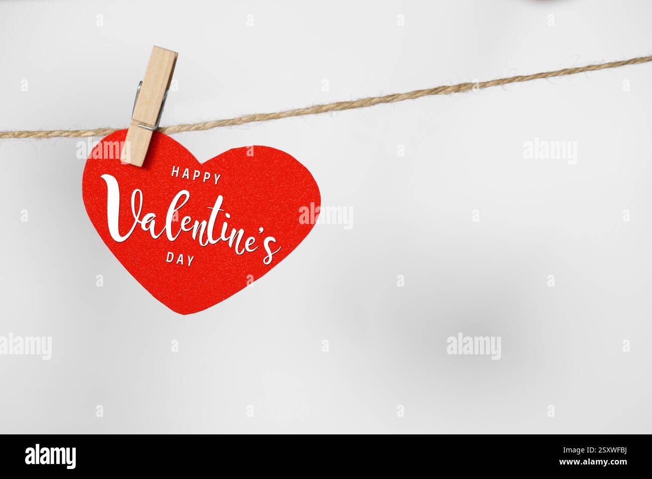 Valentine's day heart-shaped card hanging on rope against white ...