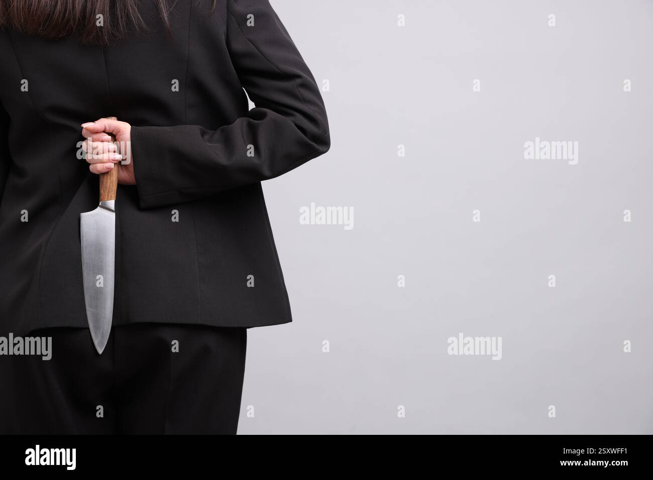 Businesswoman with knife behind her back on light grey background ...
