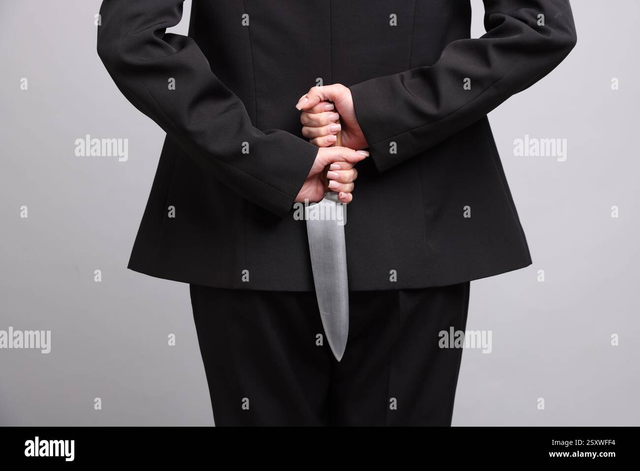 Businesswoman with knife behind her back on light grey background ...