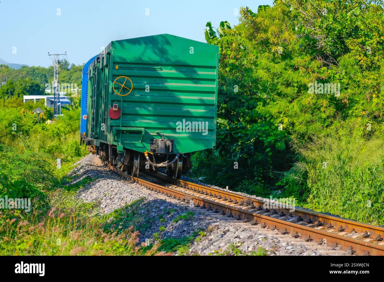 A green train carriage moves slowly along a rural railway in an area ...