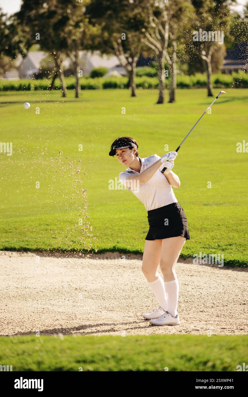Woman swinging golf club, hitting golf ball out of sand trap on sunny ...