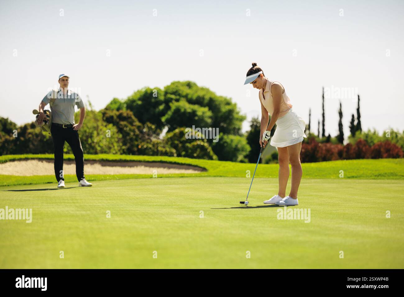 A determined woman in a putting stance aims carefully on the putting ...