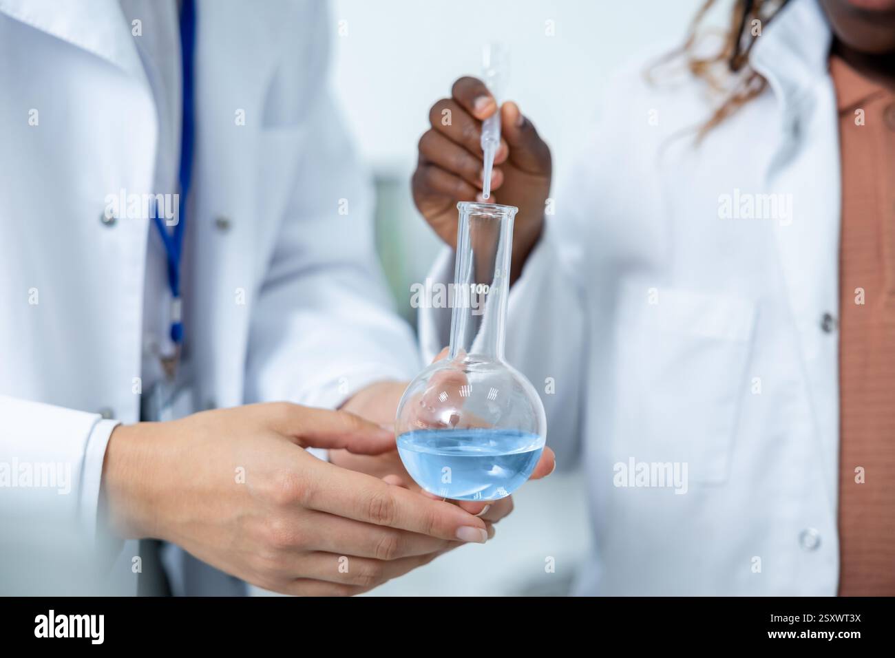 Diverse scientists' hands with flask that has blue chemical liquid ...