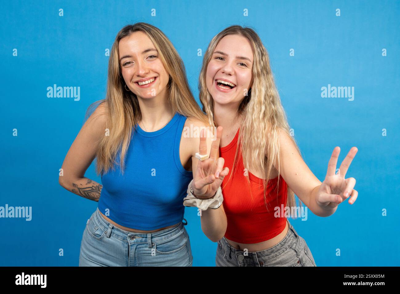 Two happy young women making peace sign with fingers, smiling and ...