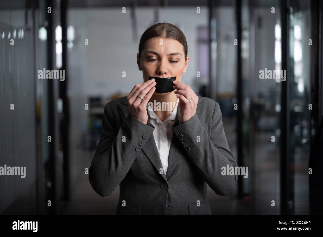 Businesswoman in formal attire covering her mouth with black tape ...