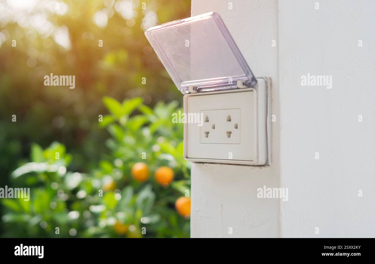 White plug on white wall with a garden in the background, plug socket ...