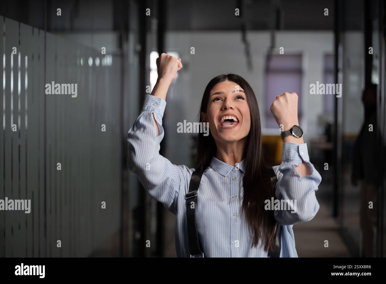 Excited young woman celebrating success in a modern office, raising her ...