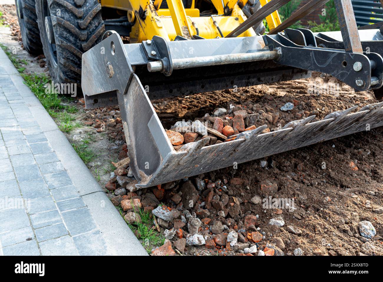 A backhoe loader carries and levels rubble on a dirt road Stock Photo ...