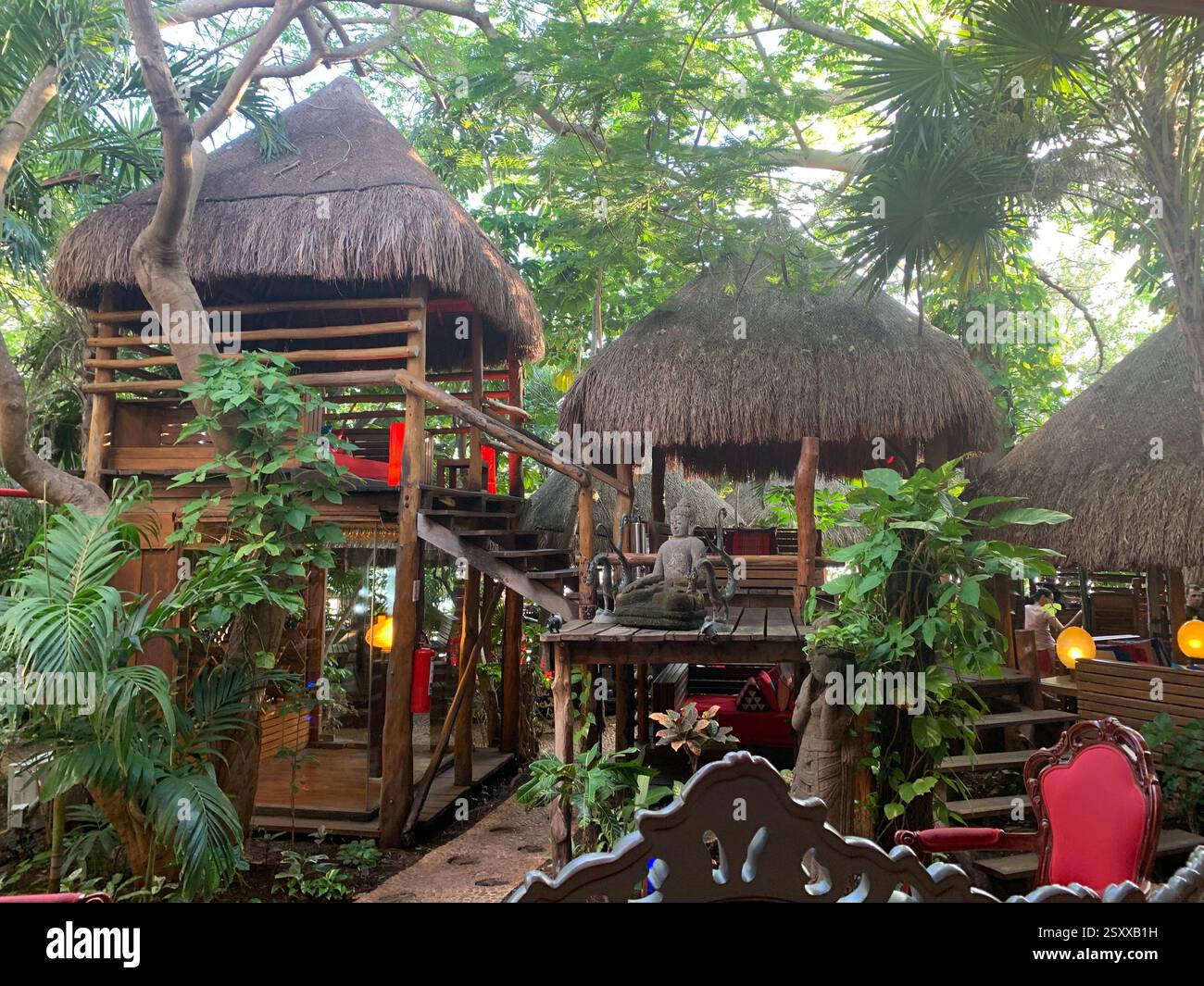 Rustic tropical treehouse-style restaurant with thatched roofs, wooden structures, and lush ...