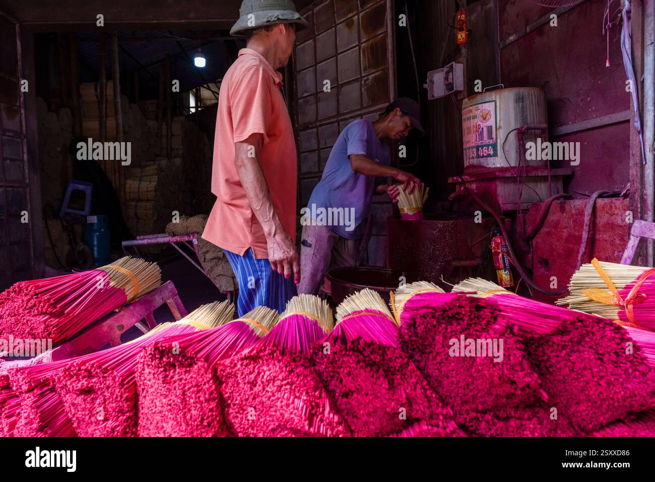 Two men dye split thin bamboo sticks with red paint for the later ...
