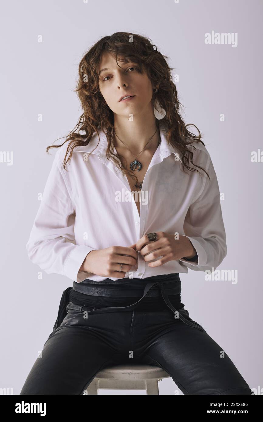 A young, handsome man sits poised, wearing a fashionable outfit in a ...